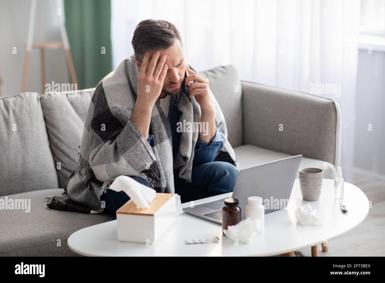 Sick man working on laptop at home, talking on phone Stock Photo - Alamy