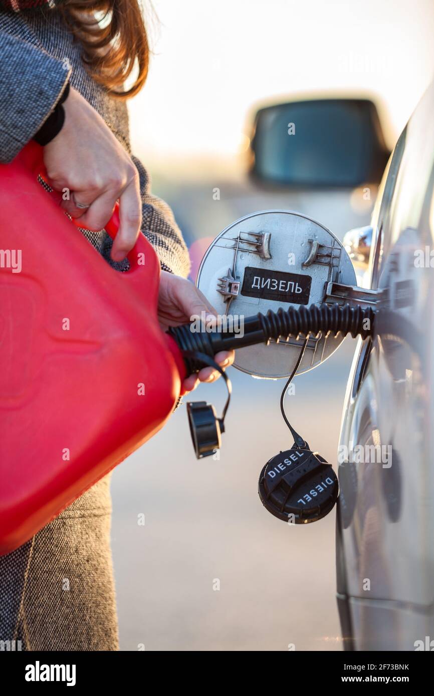 Female driver pouring diesel from red plastic oil can into empty car ...