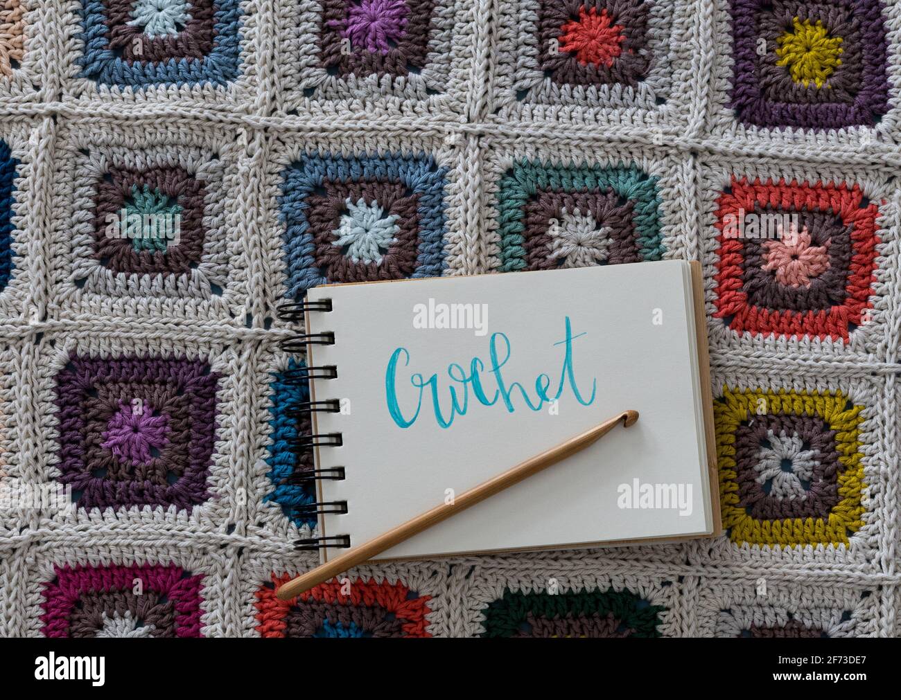 Blue word "Crochet" written in an empty spiral notebook over a granny ...