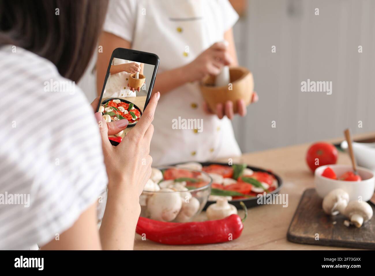 Female food photographer with mobile phone taking picture of pizza ...