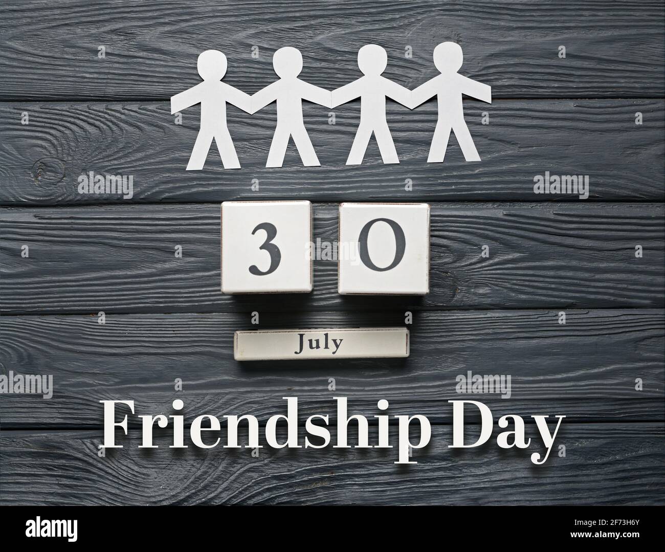 Paper human figures and calendar with date of Friendship day on wooden ...