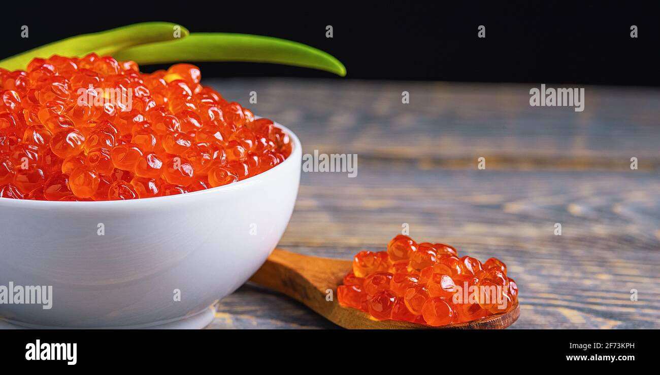 Red caviar in a wooden cup on a wooden background with a spoon. Place ...