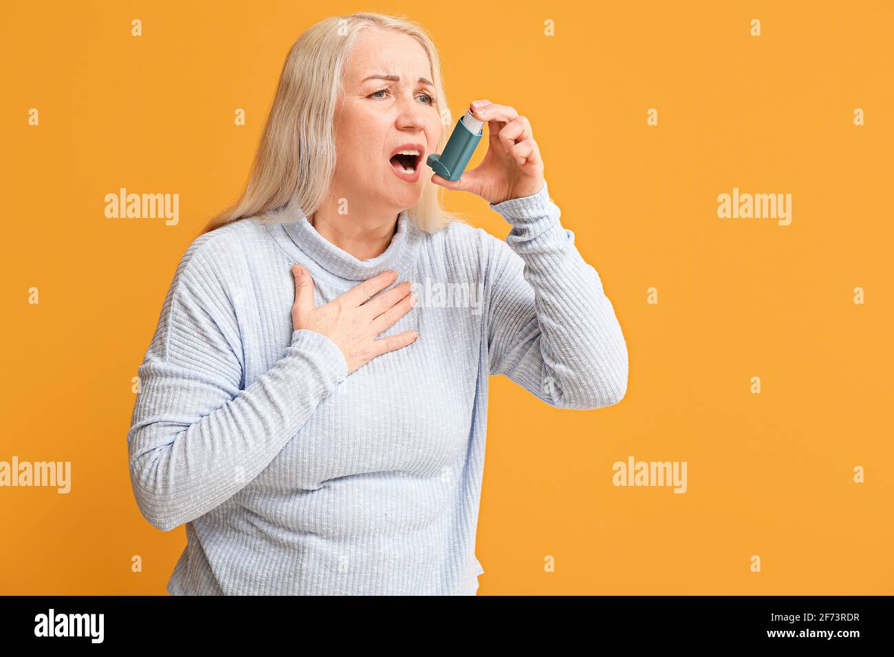 Mature woman with inhaler having asthma attack on color background ...