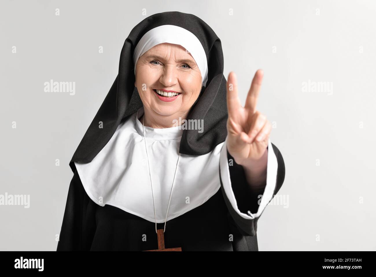 Senior nun showing victory gesture on light background Stock Photo - Alamy
