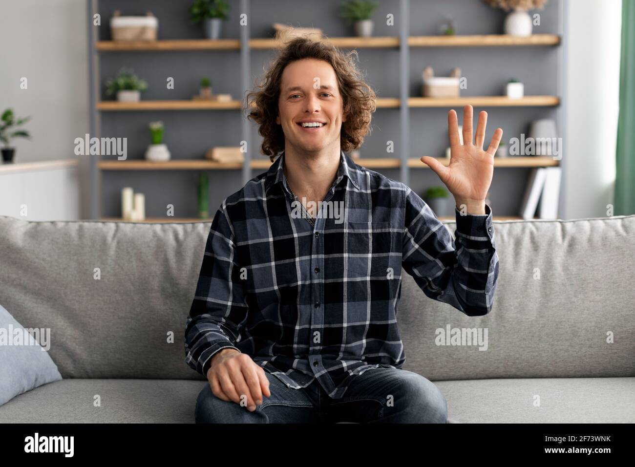 Cheerful Guy Waving Hand Sitting On Sofa At Home Stock Photo - Alamy