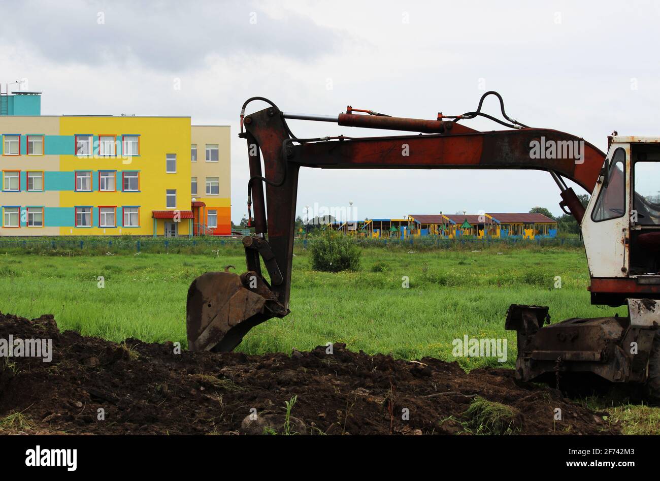 an excavator digs a ditch in a vacant lot against the backdrop of a ...