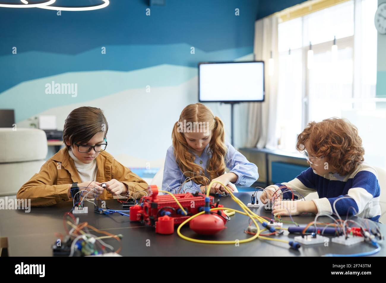 Front view portrait of three cute children building robots during ...