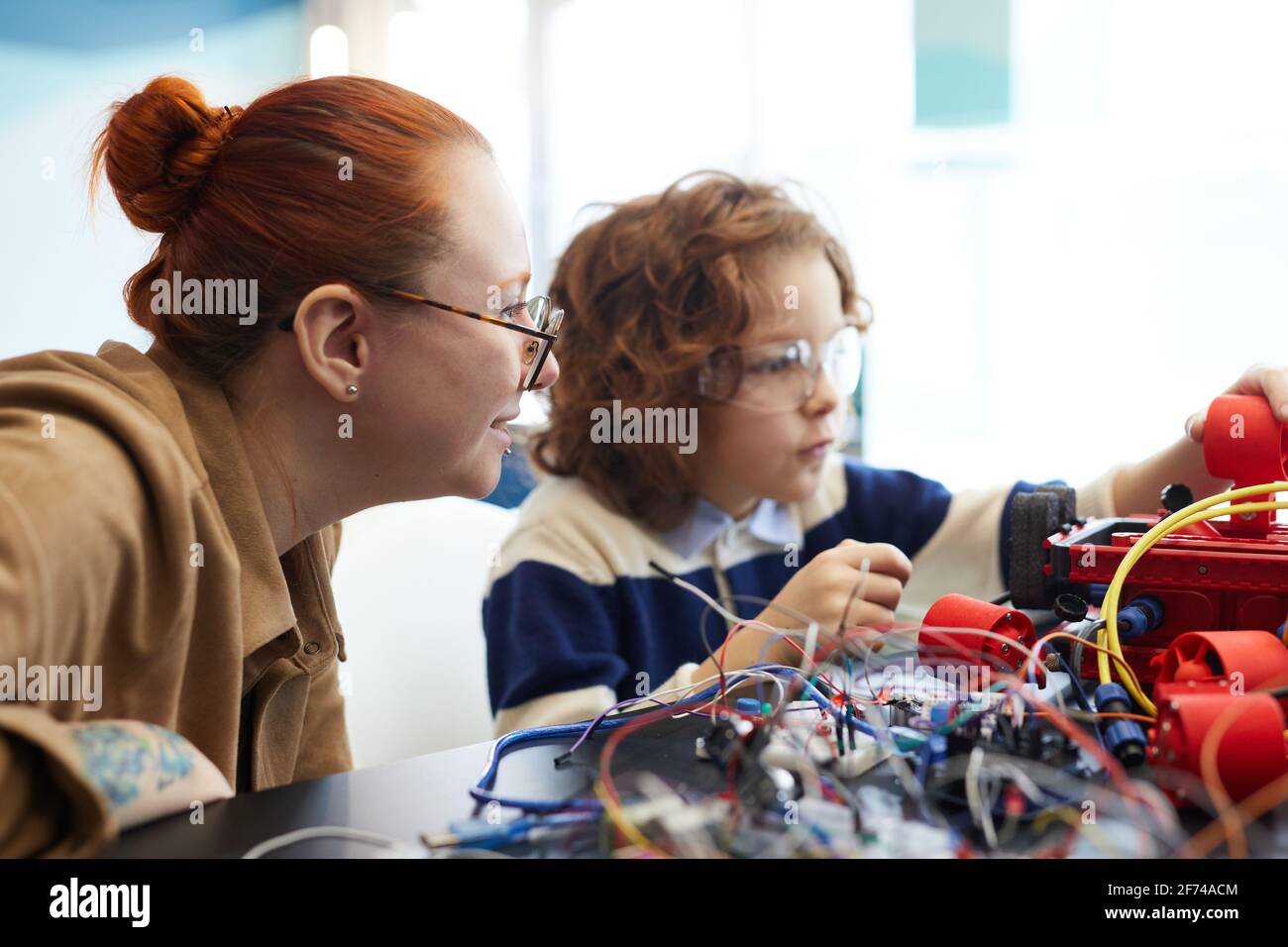 Side view portrait of female teacher helping boy building robot during ...