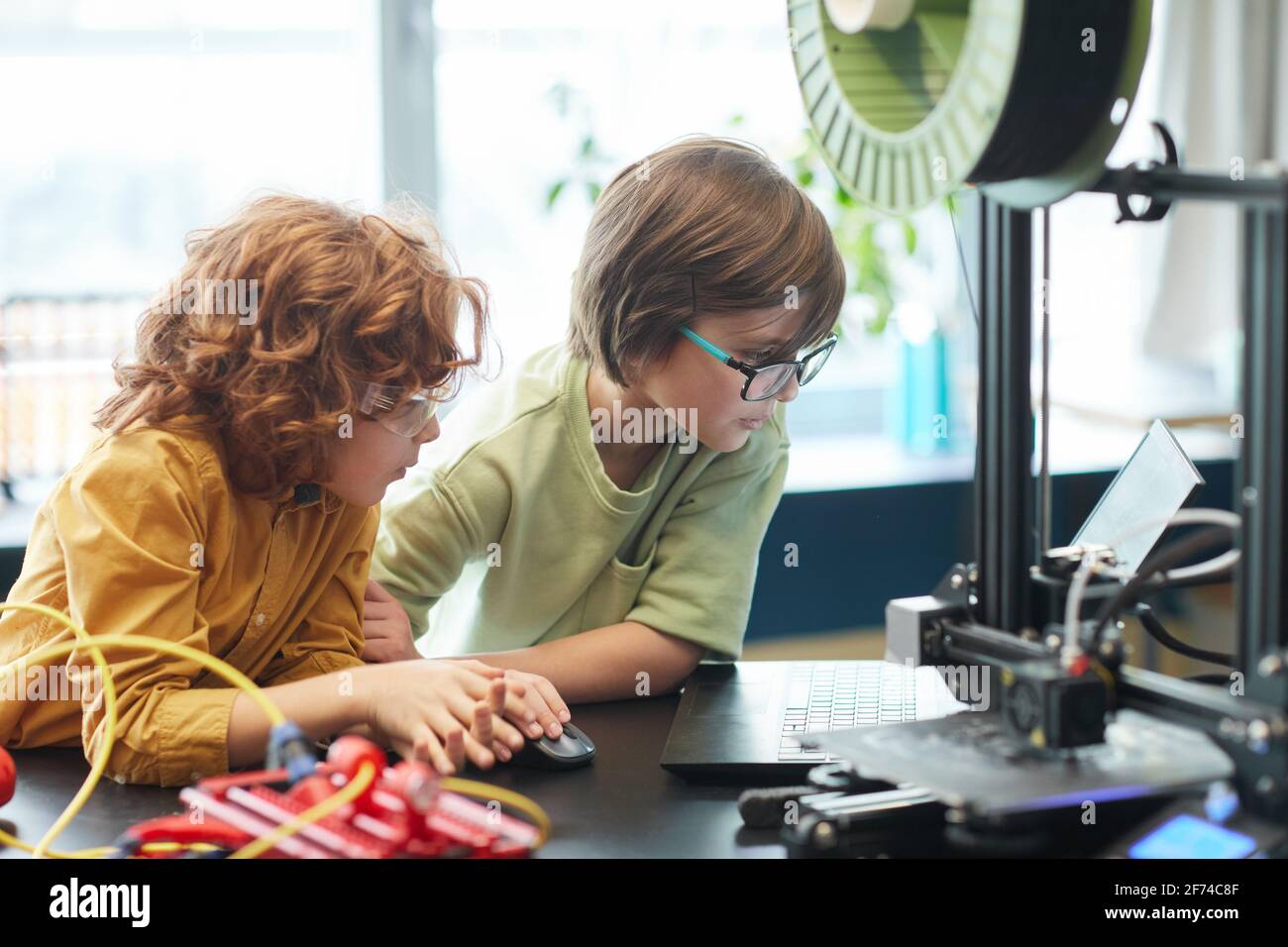 Portrait of two boys using 3D printer during engineering and robotics class at school, copy ...