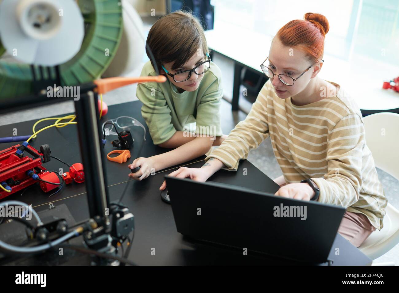 High angle view at young female teacher helping boy using 3D printer ...
