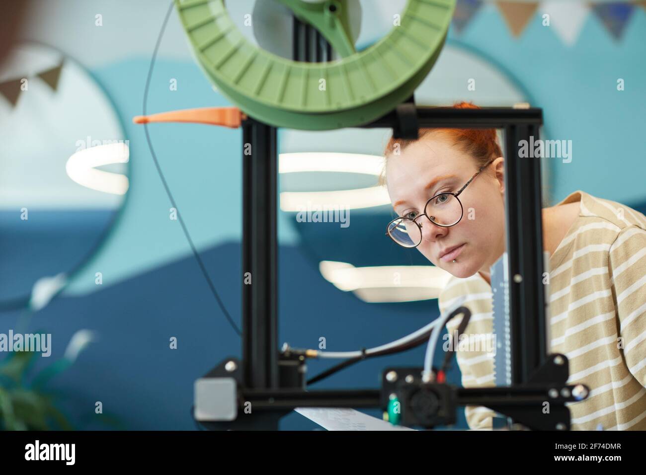 Framed portrait of young red haired woman using 3D printer in ...