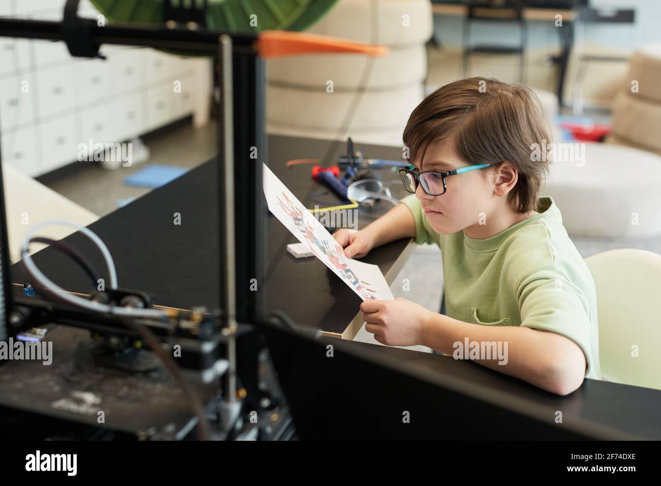 High angle portrait of little boy using 3D printer during engineering ...