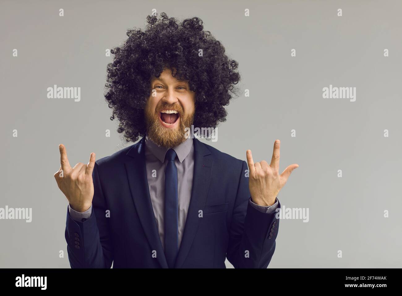 Funny crazy excited man in office suit and curly wig doing horn sign on ...