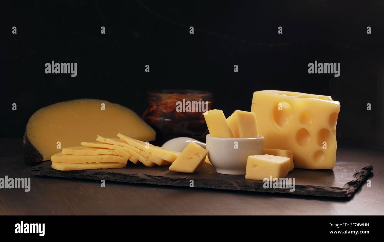 Several types of yellow cheese in chunks and cut into slices on black ...