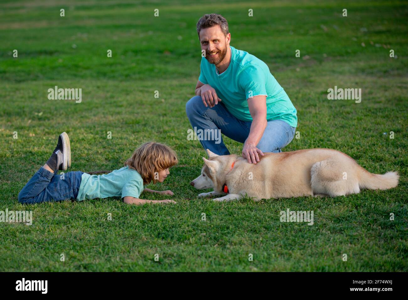 Smiling father and his son playing with dog in park with pet. Boy child ...