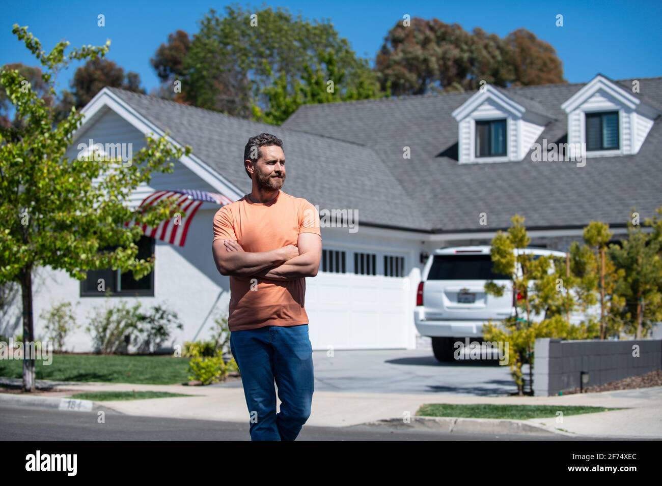 Portrait of handsome man standing outside new home. Happy guy in jeans ...