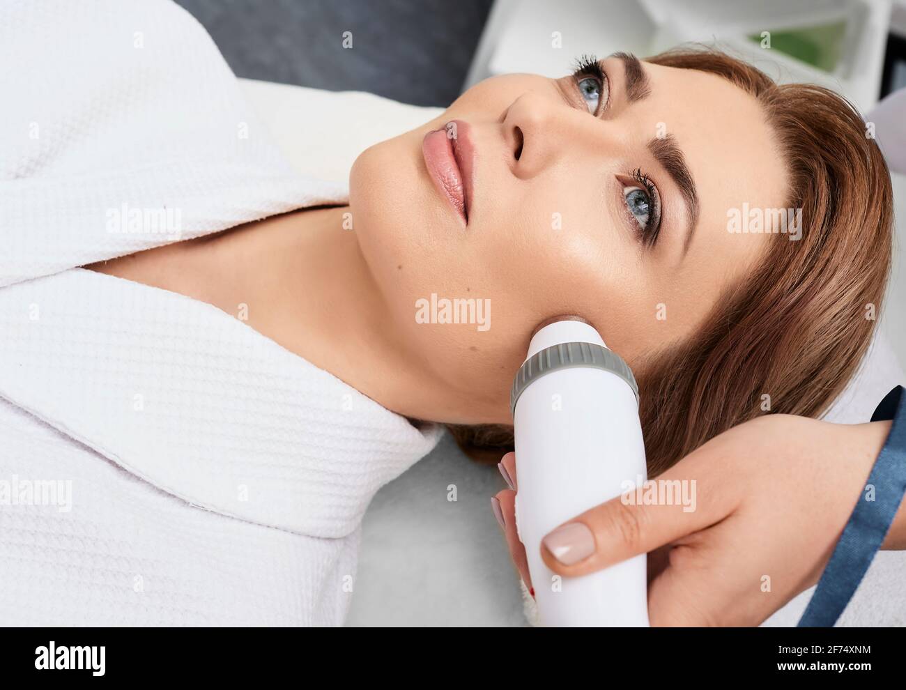 Beautician using an acoustic wave machine rejuvenates the skin of a ...