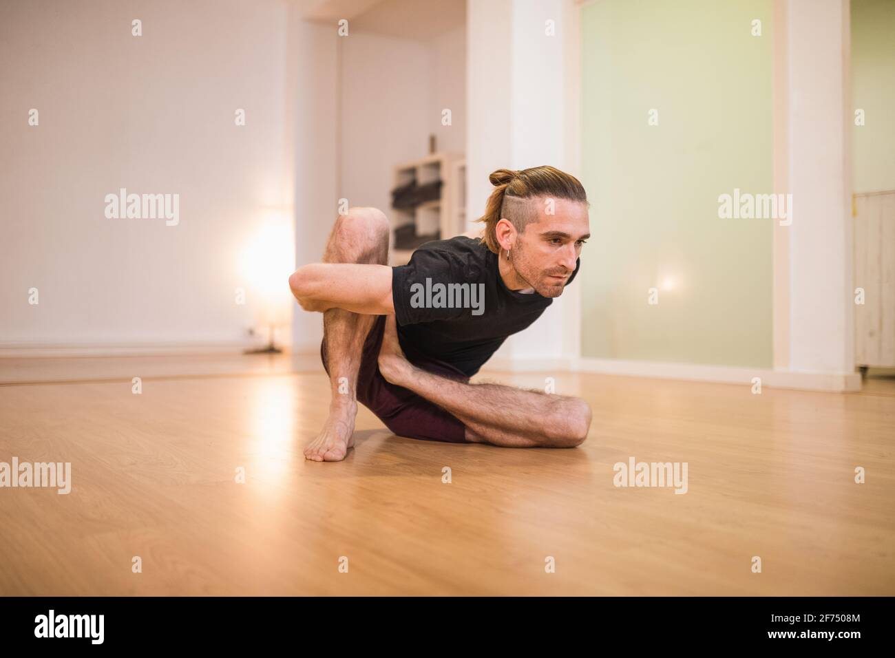 Adult male in sportswear with hands behind back performing forward bend ...
