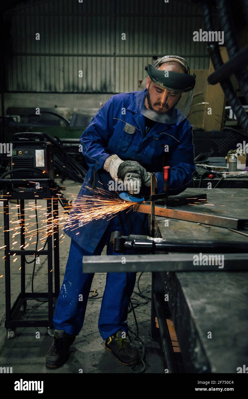 Full body of workman in protective mask and blue workwear grinding ...