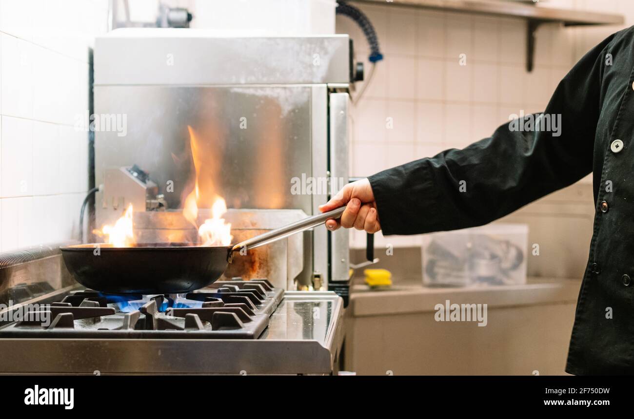 Side view of crop faceless cook preparing dish in frying pan on stove ...