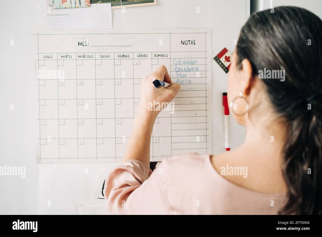 Back view of anonymous female taking notes in calendar on fridge with ...