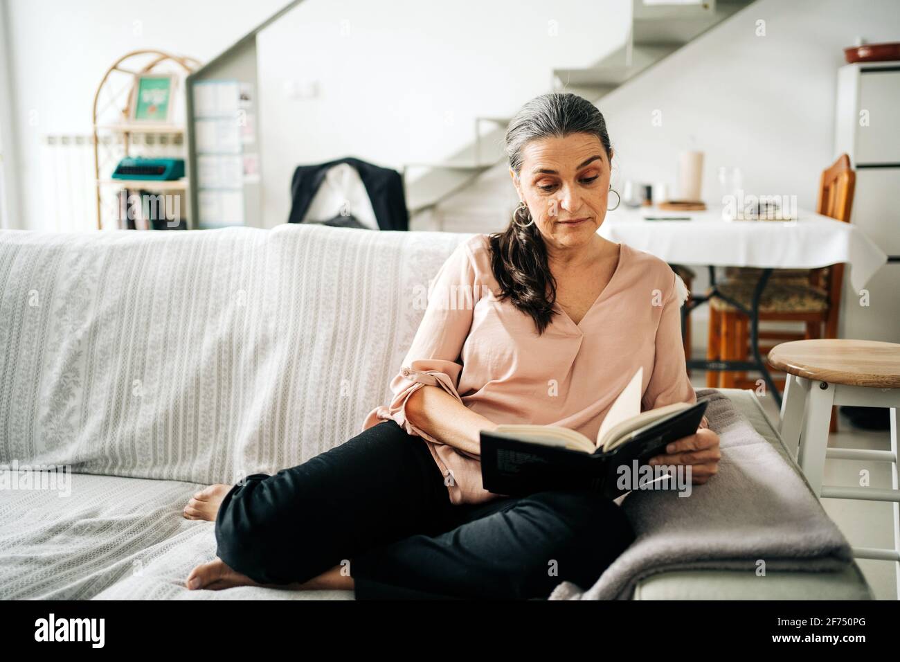 Full body of barefoot female reading book while sitting on comfortable ...