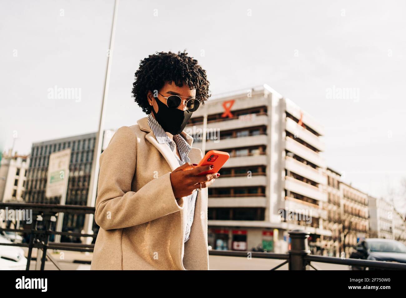 From below of stylish African American female in cloth mask texting ...