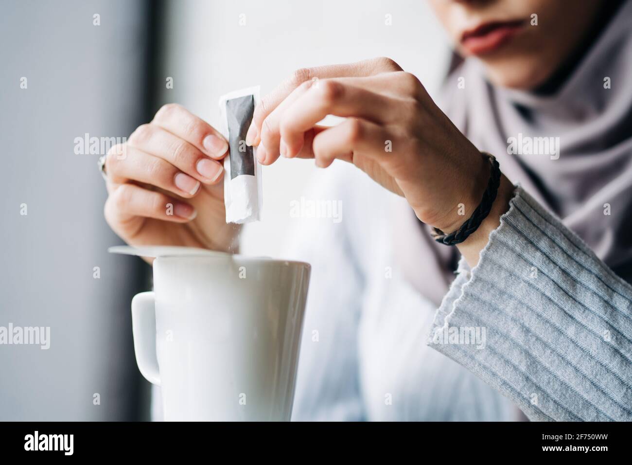 Crop anonymous Muslim female in hijab pouring sugar from paper packet ...
