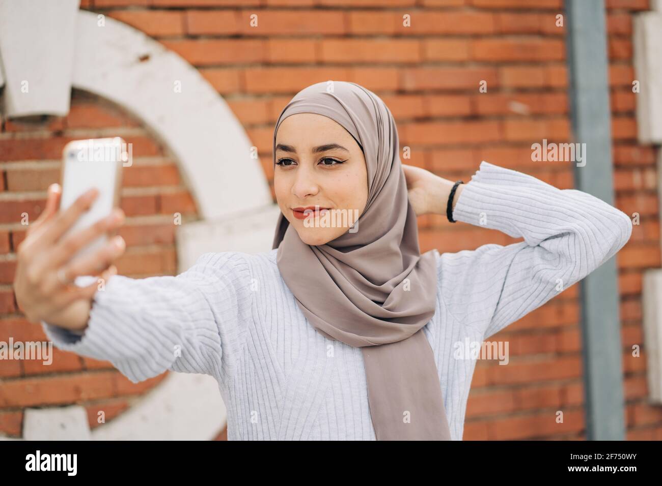 Young smiling Muslim female in traditional hijab standing on street and ...