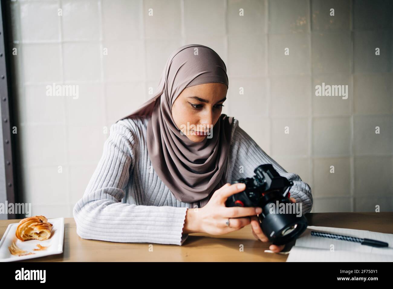 Focused Muslim female photographer sitting at table and looking through ...
