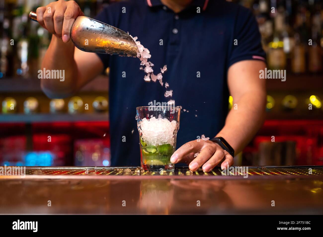 Unrecognizable bartender pouring crushed ice to the glass while preparing mojito cocktail in the ...
