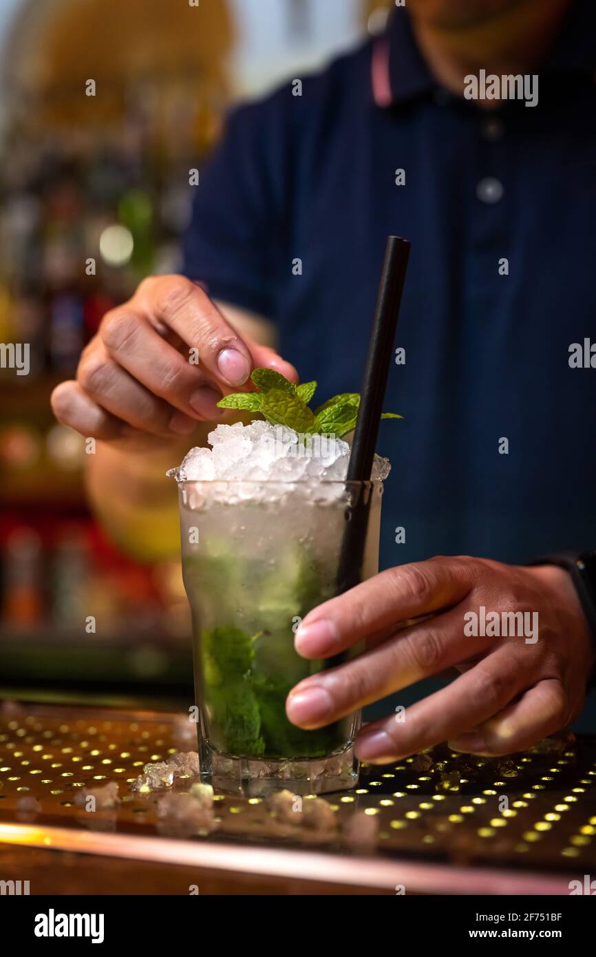 Hands of unrecognizable bartender decorating mojito cocktail with mint leaves in the bar Stock ...