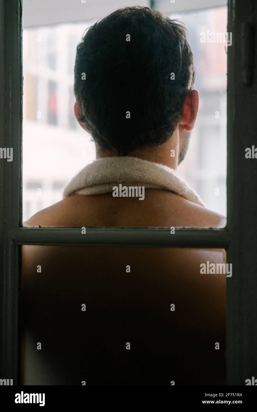 Back view of male with naked torso standing near window at home and ...