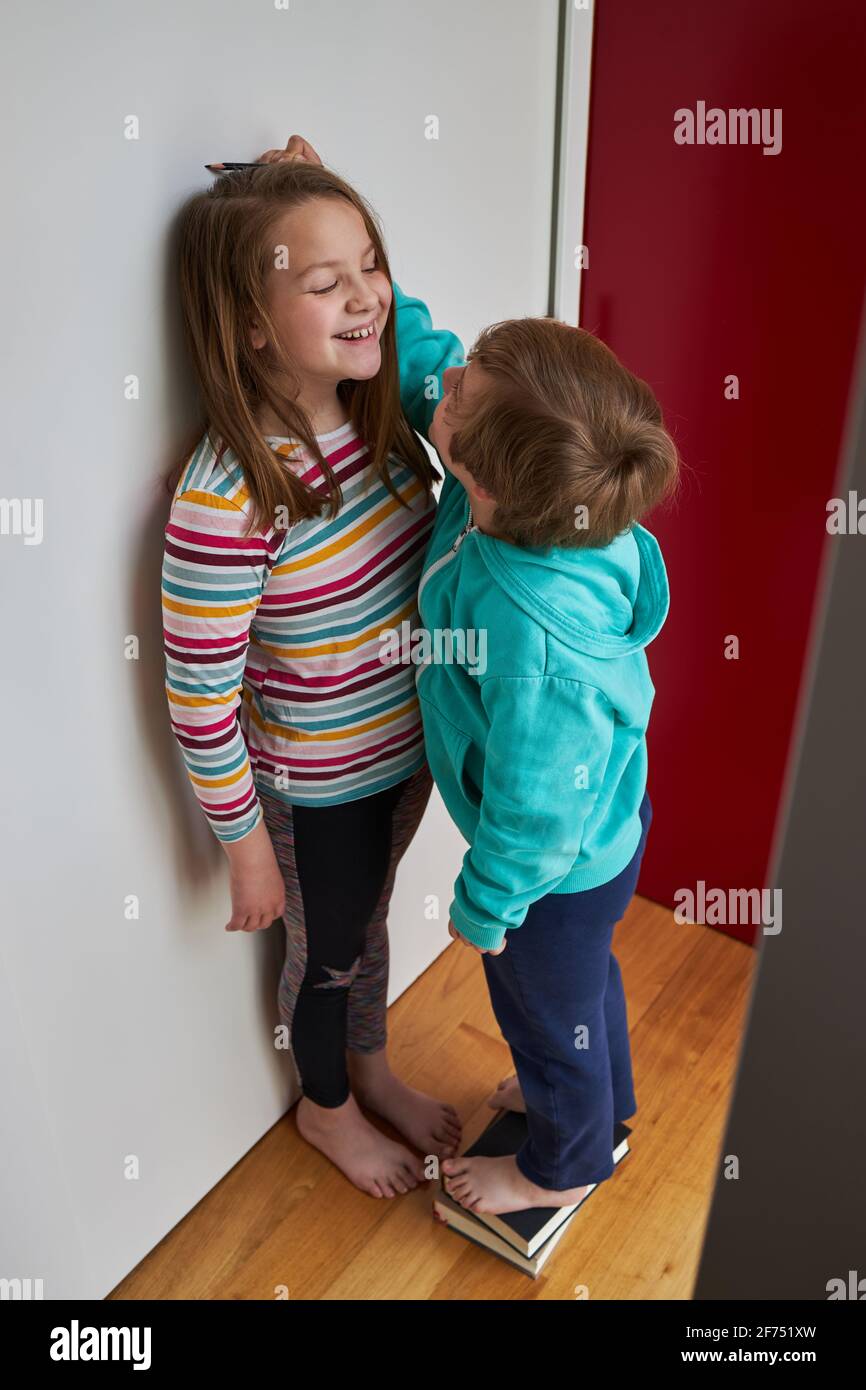 From above of brother measuring height of content sister standing near ...