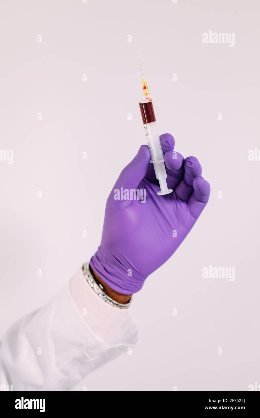 Crop anonymous doctor in medical glove demonstrating syringe with blood ...