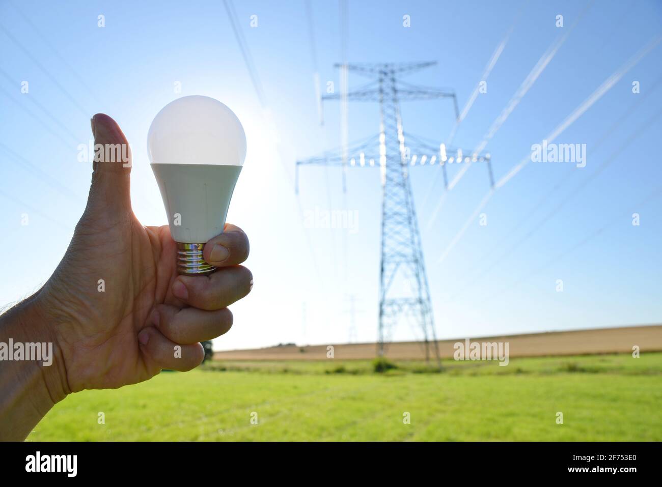 Hand holding eco LED light bulb with transmission tower at the ...