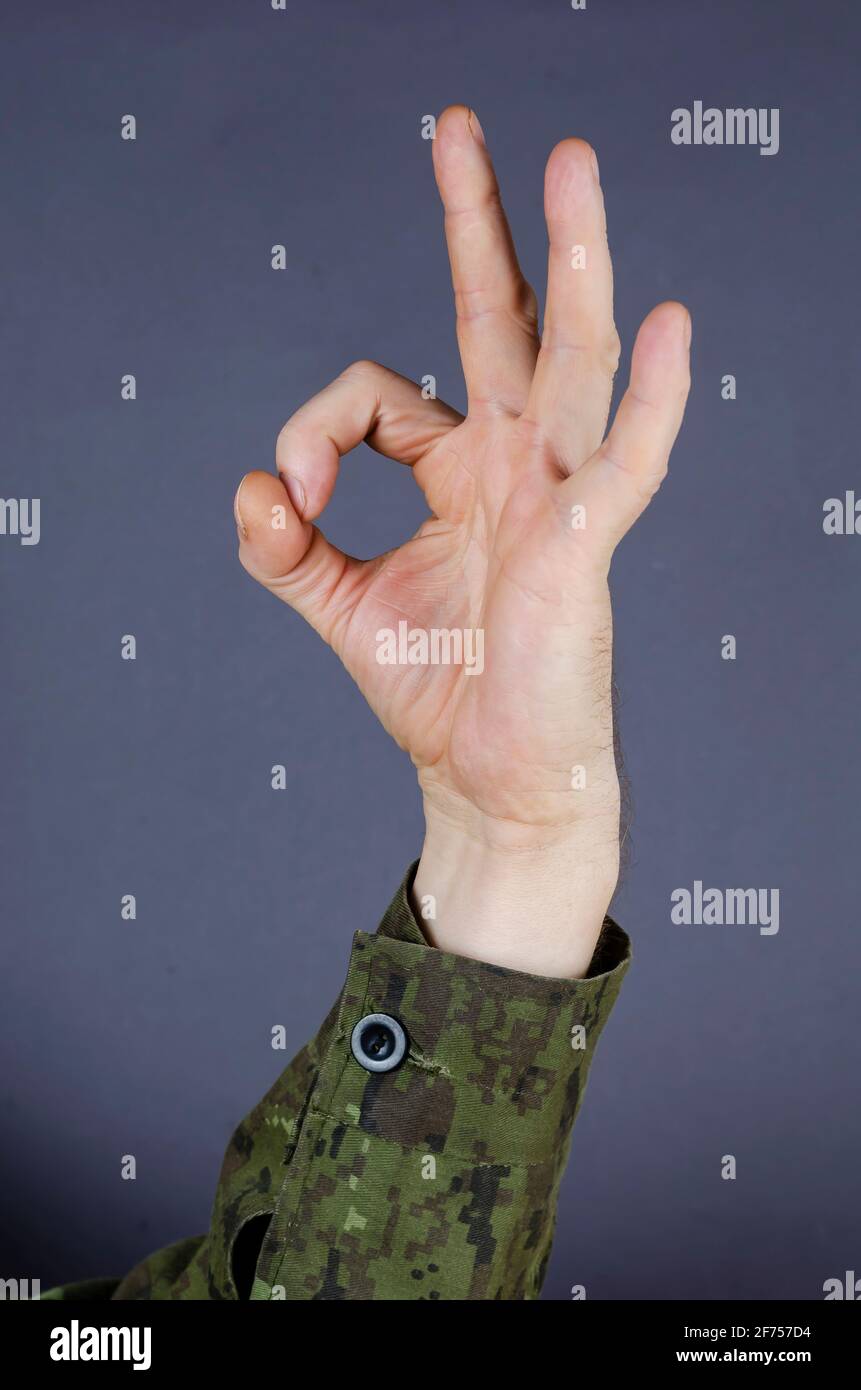 Hand in camouflage shows gesture with his fingers on gray background ...