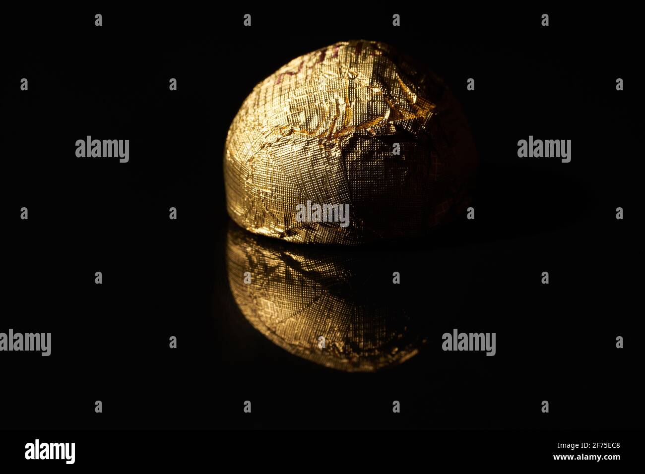 A whole chocolate candy in a golden wrapper on a black background with ...