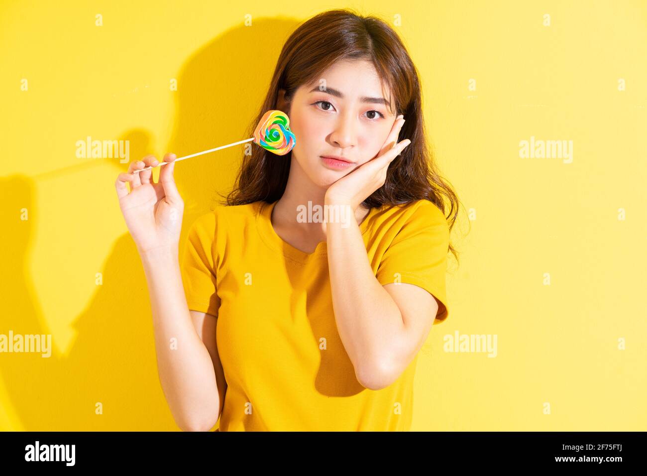 Young Asian woman eating lollipop on yellow background Stock Photo - Alamy