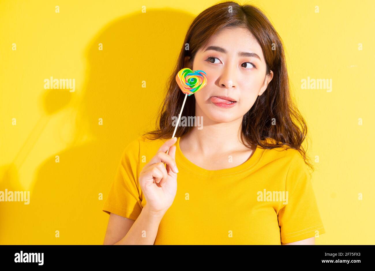 Young Asian woman eating lollipop on yellow background Stock Photo - Alamy