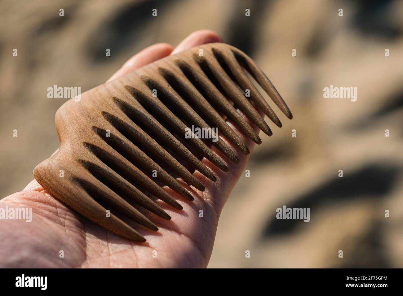 Wooden comb on a palm at sand background. Tool for scalp massage and ...