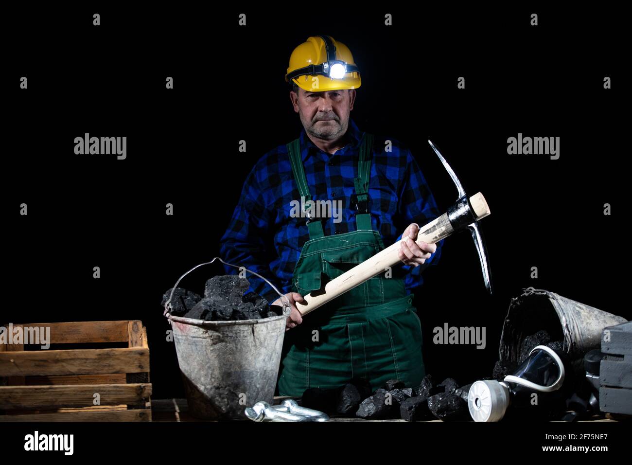 A miner with a pickaxe in his hand stands by a bucket full of black ...