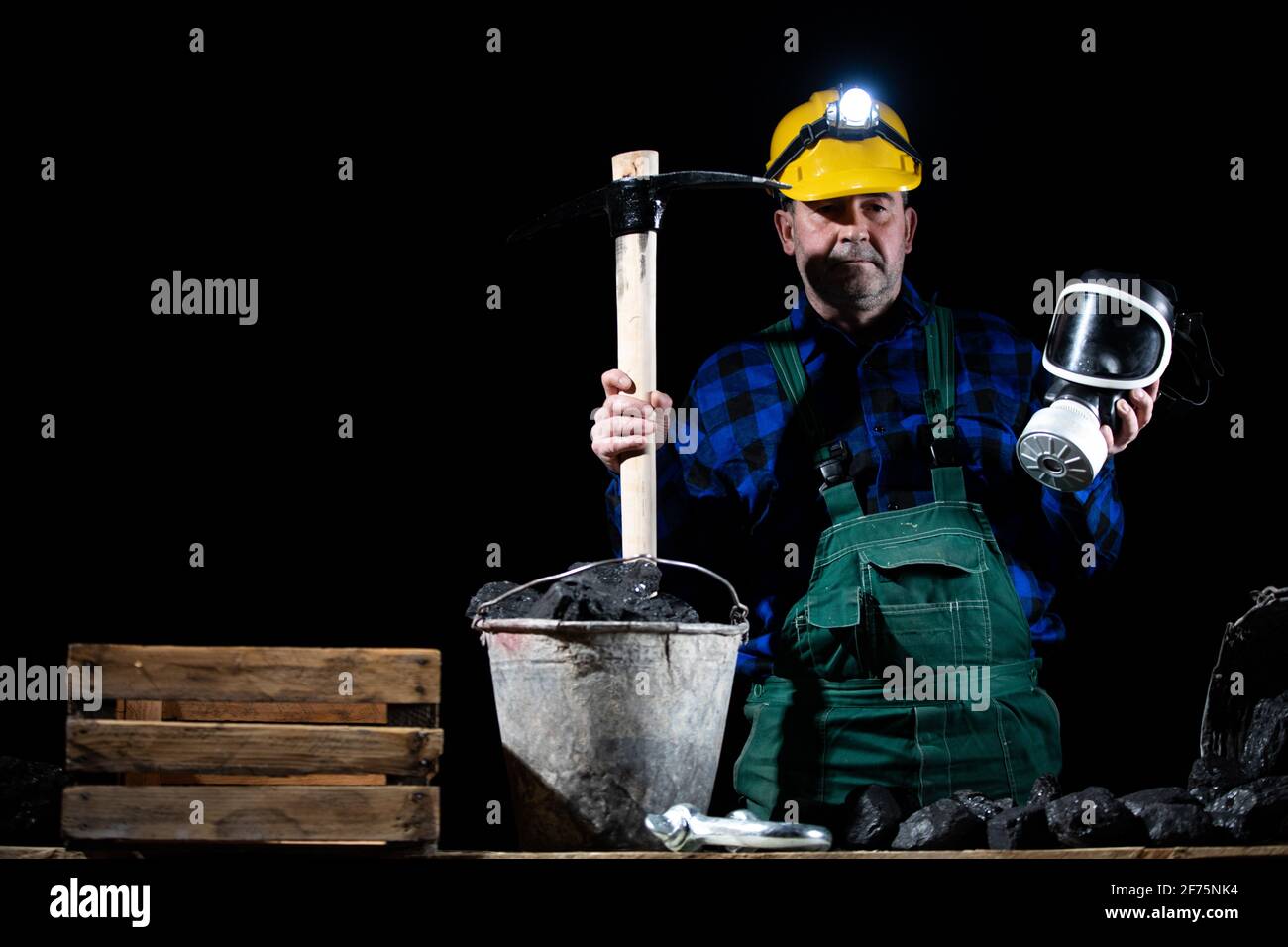 A miner stands holding a pickaxe in one hand and a dust mask in the ...