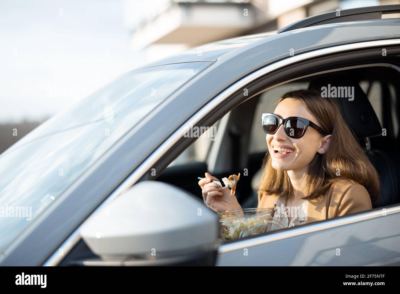 Beautiful woman eating heathy salad in the car. Received a food order ...