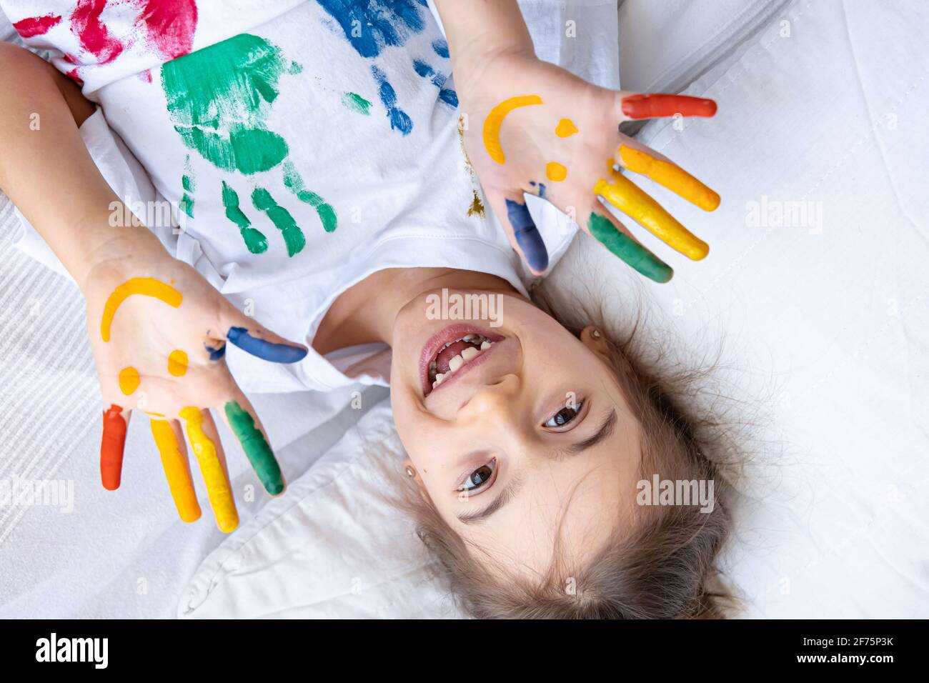 Painted smiles on the palms of a little girl in a T-shirt with colored ...