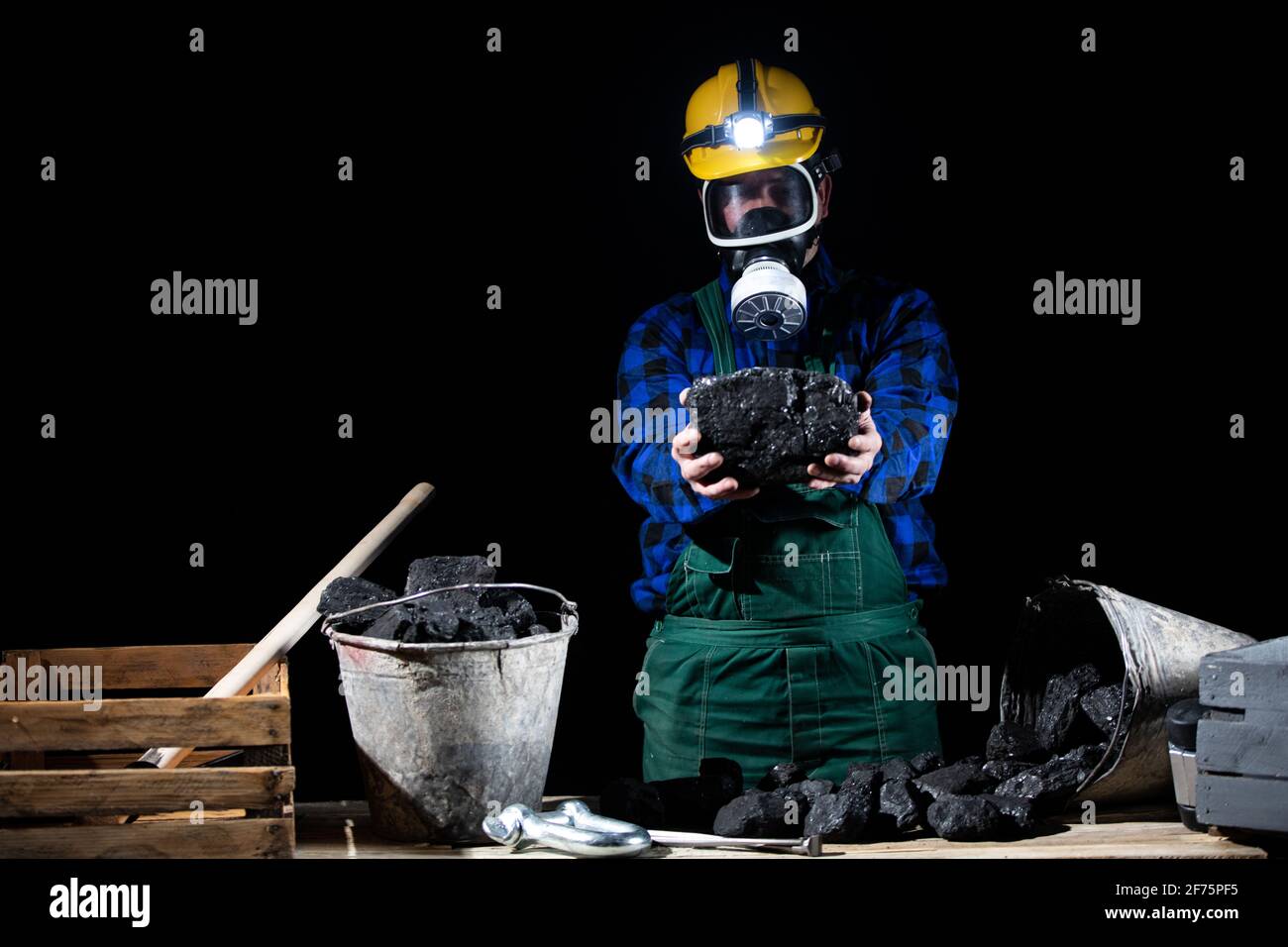 A miner in a helmet with a glowing flashlight and a dust mask on holds ...