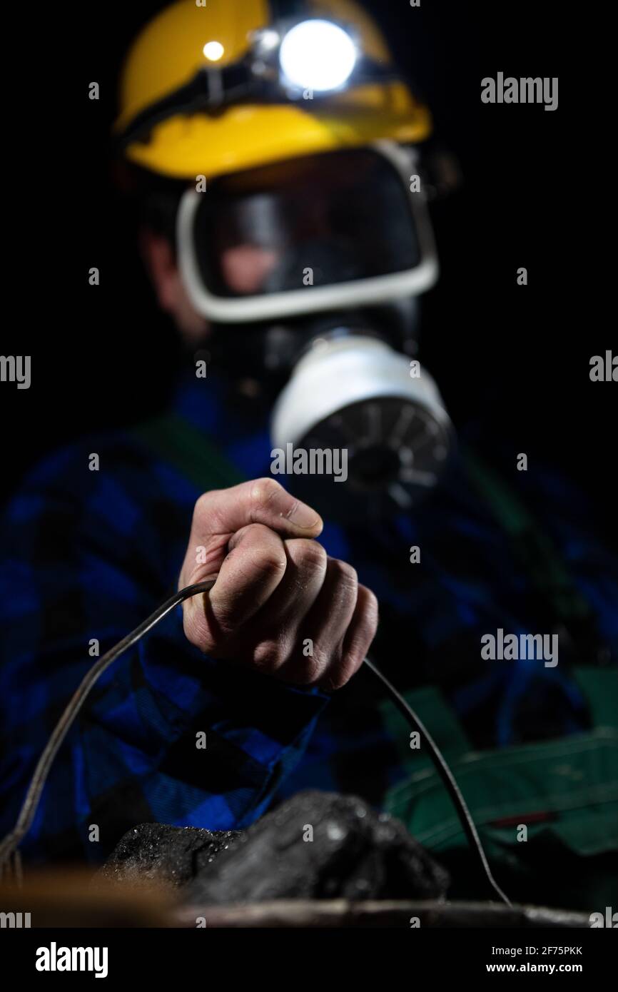 A miner wearing a helmet with a flashlight and a dust mask holds a ...