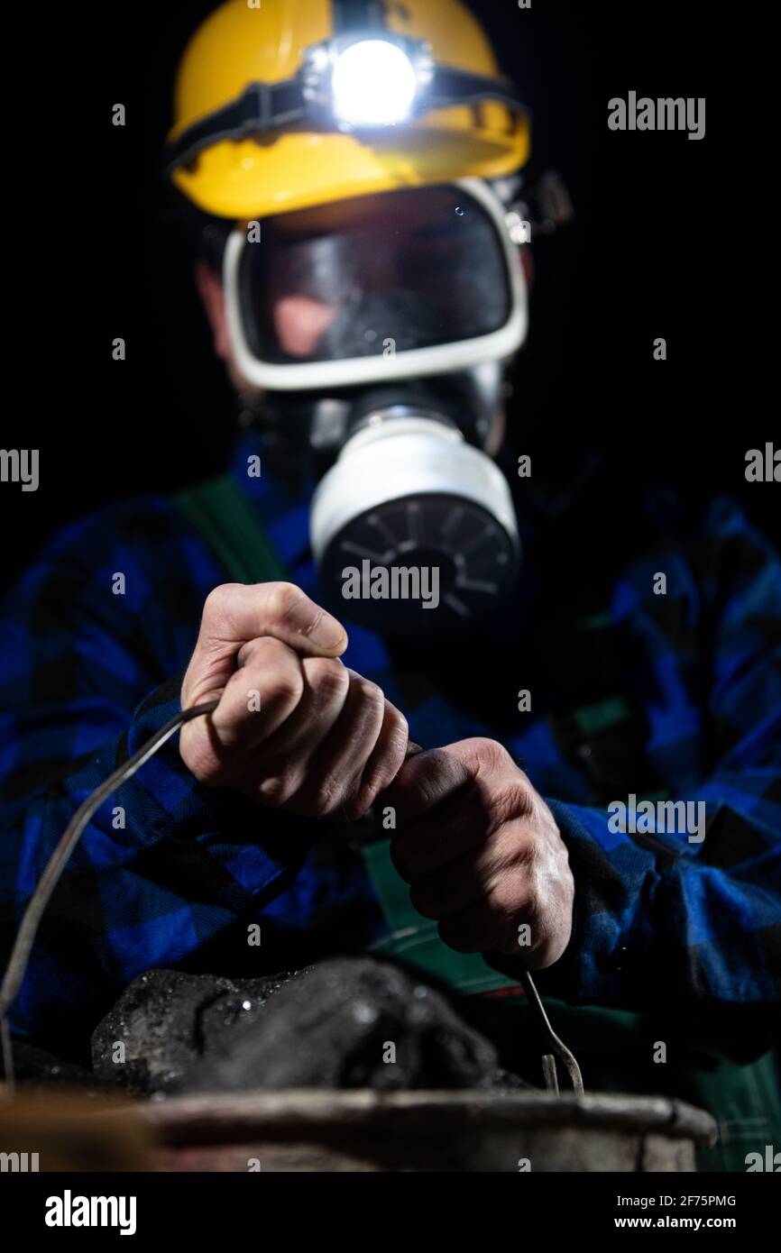 A miner wearing a helmet with a flashlight and a dust mask holds a ...