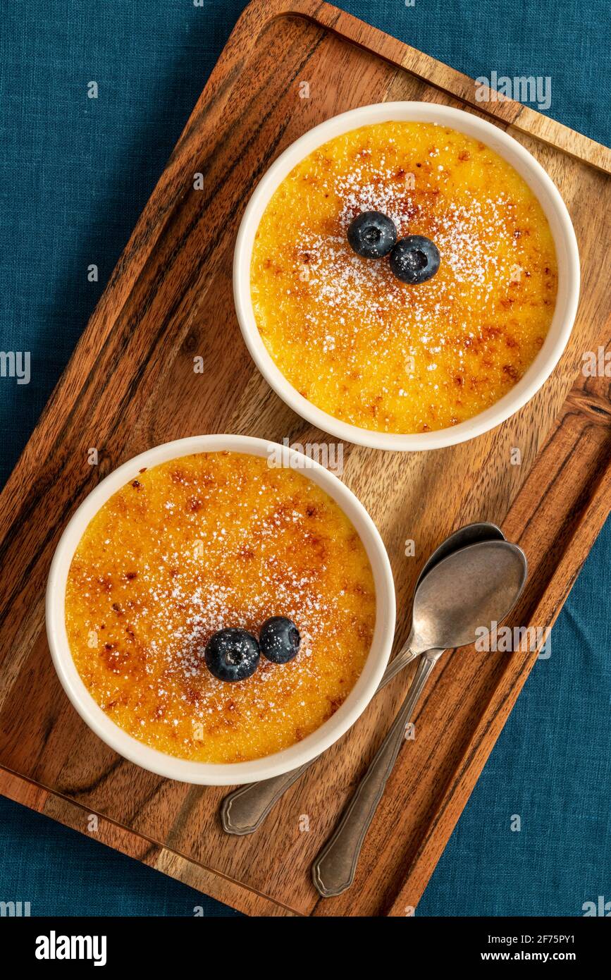 Creme brulee in ramekin on wooden tray on dark linen tablecloth. Close ...