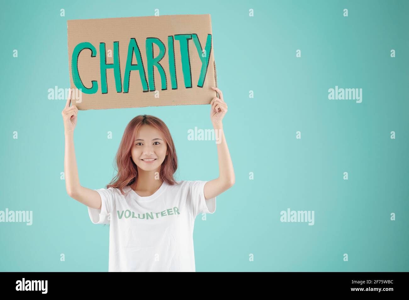 Smiling pretty young female volunteer holding charity paper sign above ...